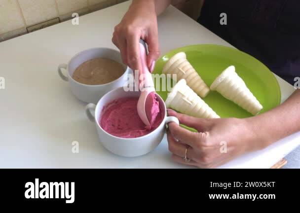 A woman fills the horn with strawberry ice cream. Using an ice cream ...
