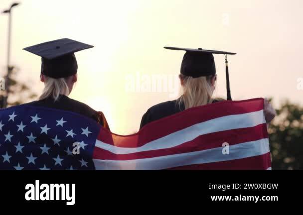 Two women college graduates raise their hands up, on the shoulders of ...