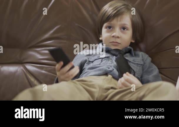 The little cute boy sitting on the leather sofa with legs apart ...
