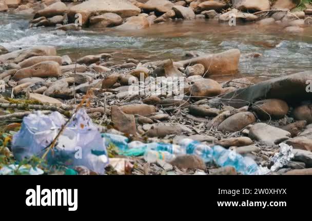 Mountain fast clean stream, on rocky shore, which has garbage, plastic ...
