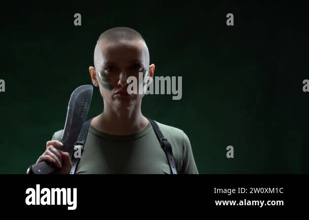 Angry bald girl with camouflage makeup shaving machete hair on a black ...