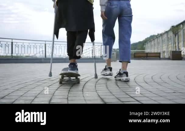 Young man with one leg on crutches riding on skateboard walking with ...