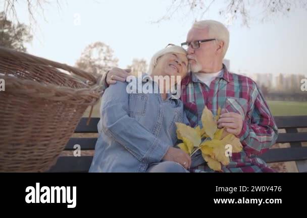Happy Caucasian mature family sitting on the bench in sunlight and talking. Senior European ...