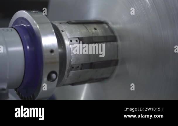 Extreme close-up of automated machinery rolling aluminium foil sheet ...