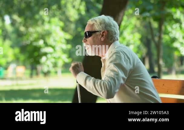 Blind man standing up from bench after rest and going for walk along ...