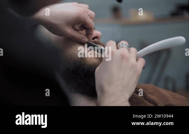 Barber shaves men with a long beard with straight razor blade in s hair ...