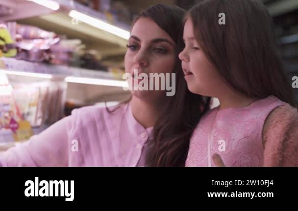 Mom and daughter choose food on the shelf at the grocery store. Little ...
