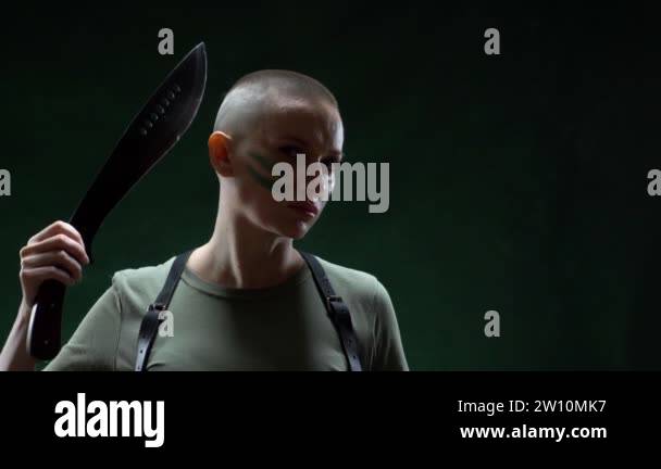 Angry bald girl with camouflage makeup shaving machete hair on a black ...