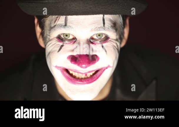 Scary man in a clown makeup looks at the camera and laughs. A scary ...