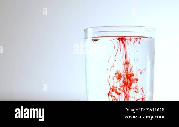 small particles of red substance fall into a transparent glass with ...