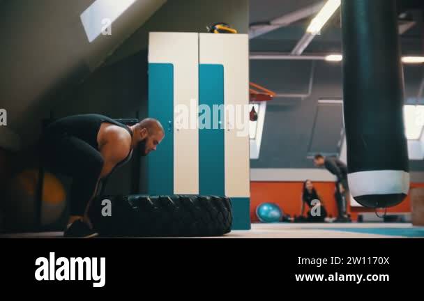 A bearded man bodybuilder flips a tire on the floor over and over in ...