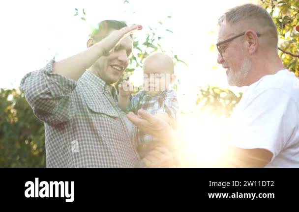 Grandfather, son and grandson clap each others hands, teach the baby to ...
