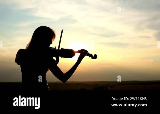 Silhouette girl violinist playing the violin at sunset sky background ...