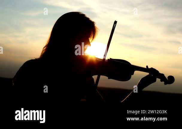 Silhouette girl violinist playing the violin at sunset sky background ...