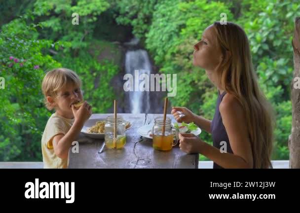 Young woman and her little son have a lanch in a cafe with an epic view ...
