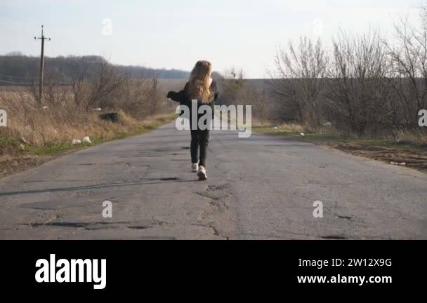 Rear view of little girl in jacket walks along empty road and dancing ...