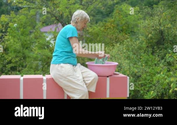 Old woman washing clothes in a pink plastic basin on nature green ...