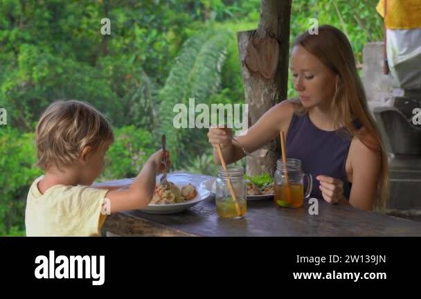 Young woman and her little son have a lanch in a cafe with an epic view ...