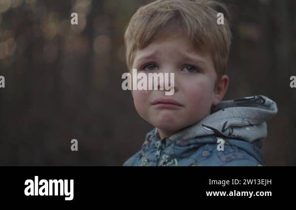 Upset boy in jacket crying with tears in sunset fall park in slow ...