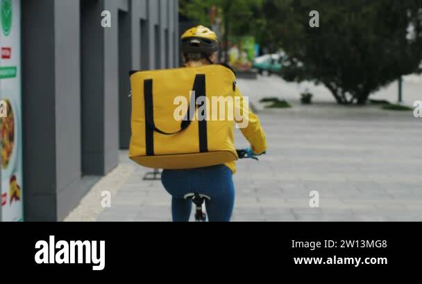 Rear of Caucasian female courier with big bag over back in casque ...