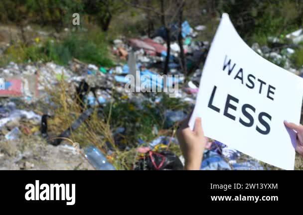 Waste less phrase on cardboard in hands against landfill background ...