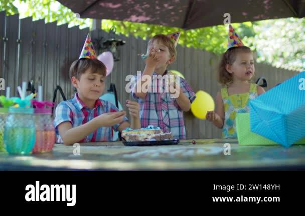 Three happy kids in party hats eating birthday cake with hands outdoors ...