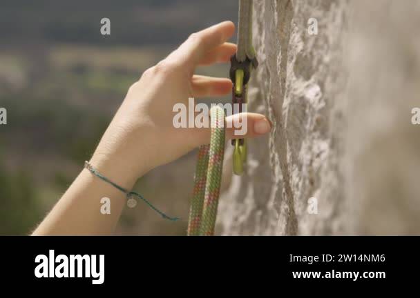 CLOSE UP, DOF: Fit woman top roping loops her rope into a safety ...