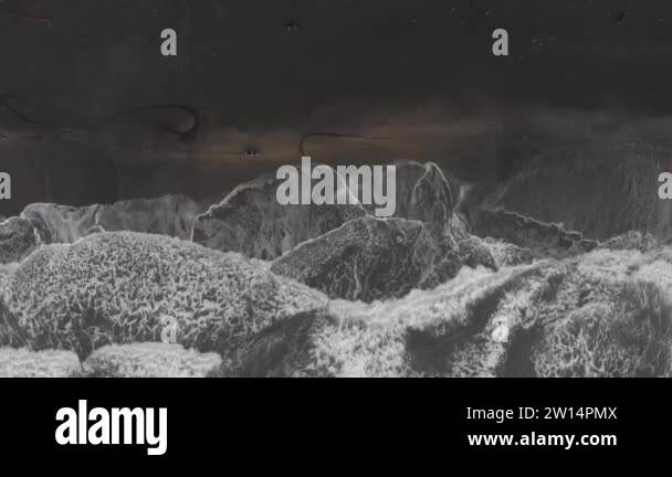 Bird's-eye view a guy on a motorcycle rides along a black sand beach ...