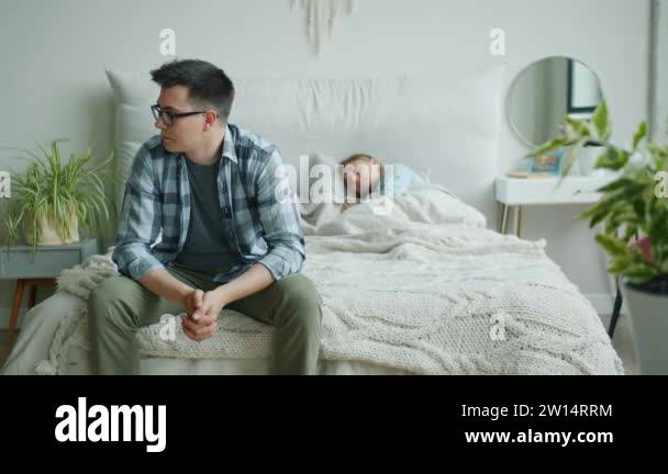 Worried Guy Sitting On Bed Touching Sad Face While Wife Sleeping At