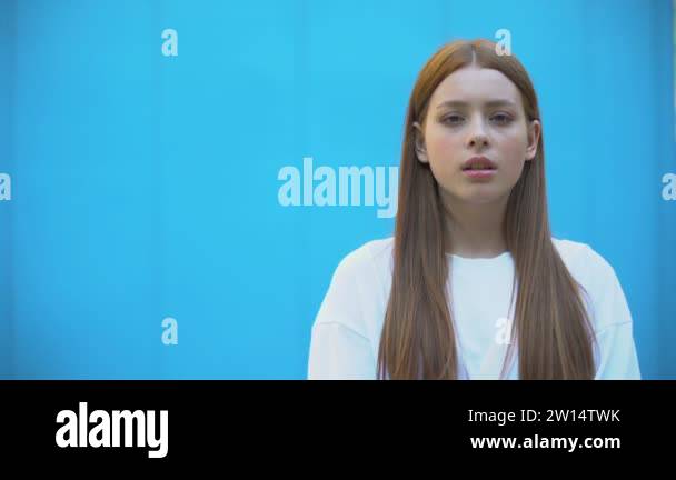 Serious teenage girl posing before camera blue background, awkward age ...