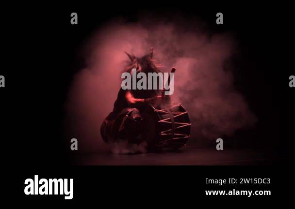 Taiko drummer in a wig and a demon mask on stage with drum on a black ...