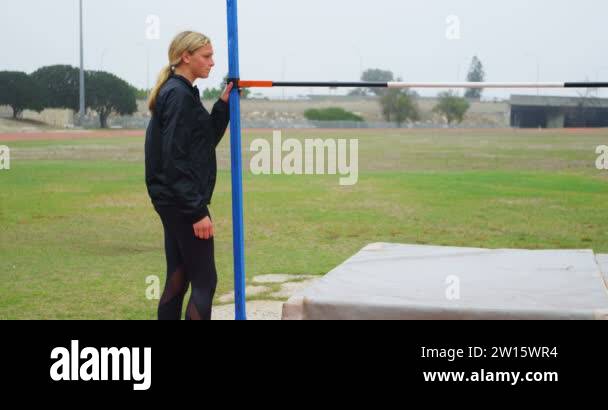 Side view of Caucasian female athlete checking high jump bar at sports ...