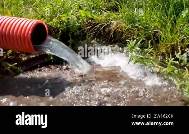 water from a red corrugated pipe flows down the drain. Water is flowing ...