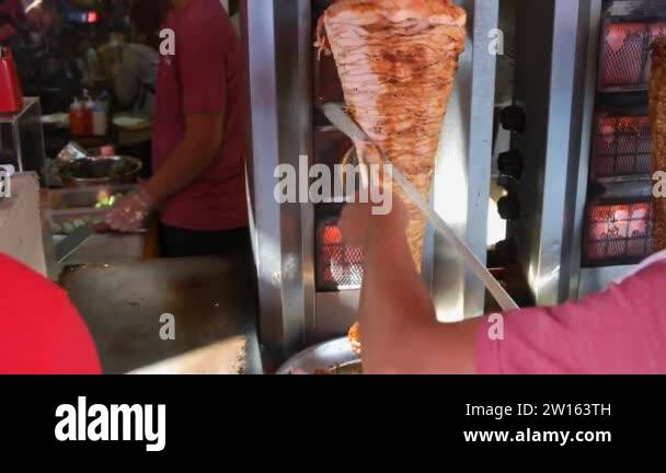 A man slicing seasoned chicken meat from a vertical rotating spit ...