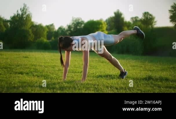 Woman athlete involved in fitness in park, doing leg lifts on mat ...