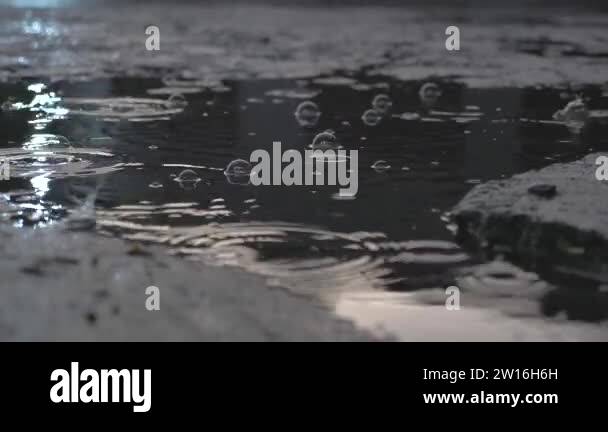 Drops of rain water fall into a large puddle on the pavement, flooding ...