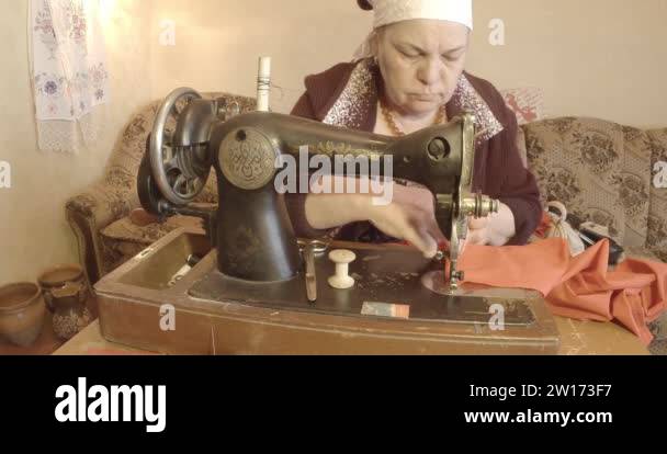grandmother sews a red flag on an old sewing machine of the Soviet ...
