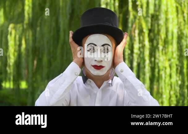 Mime in a black hat on the park shows pantomime. Mime closes her ears ...