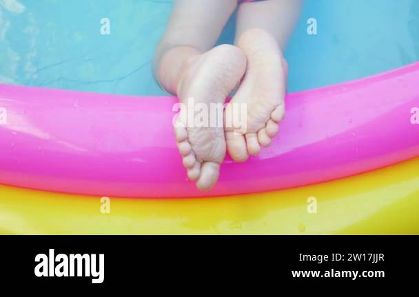 Kids feet laying on colorful rainbow inflatable swimming pool. Young ...