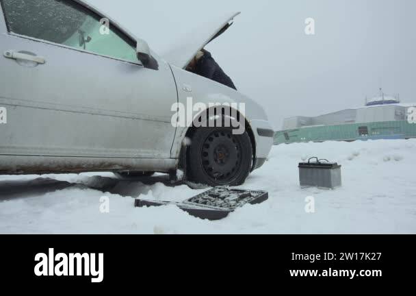Man repairs or fixes broken car in winter snowfall. Malfunction or ...