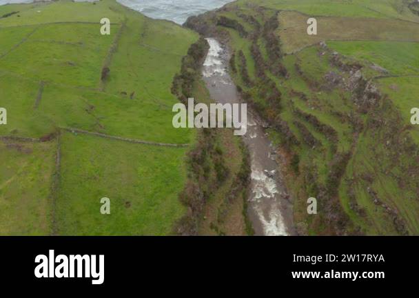 River in gorge between green fields falls as waterfall into the sea ...