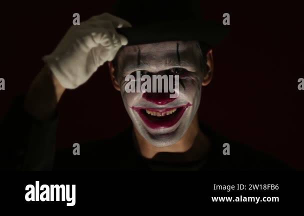 Terrible man in a clown makeup takes off his hat by welcoming his ...