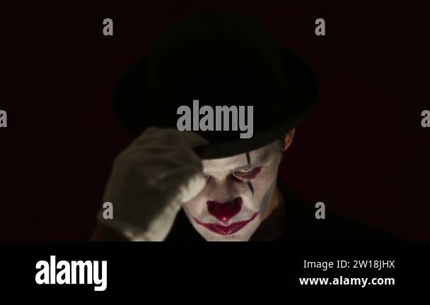 Terrible man in a clown makeup takes off his hat by welcoming his ...