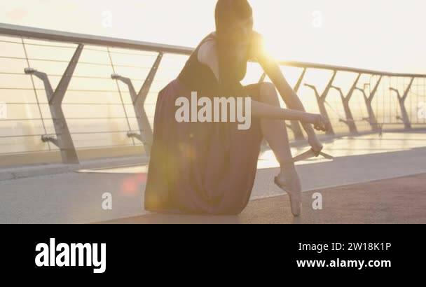 Caucasian ballerina tying up pointes in sunrays in the morning ...