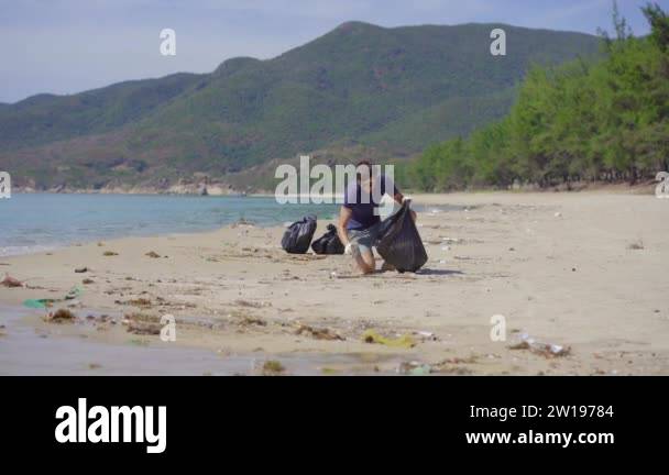 Man in gloves collects plastic trash on a beach. The problem of garbage ...