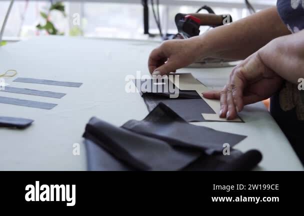 Close-up: A seamstress woman steams a piece of dark cloth as gluing ...