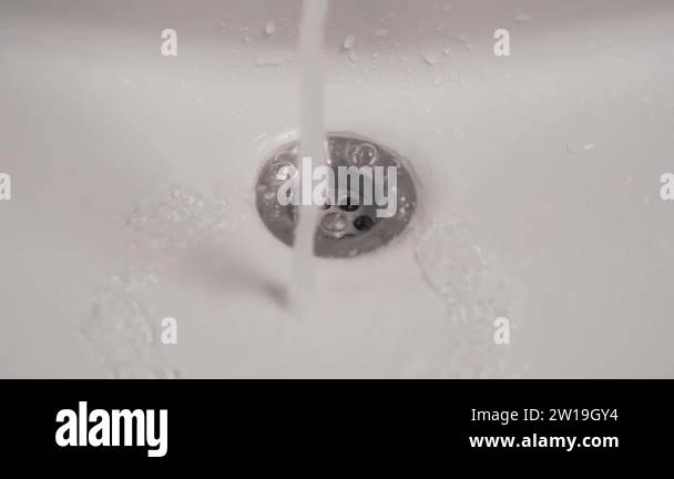 Water drips and then flows in a white sink, flowing into a hole with a ...