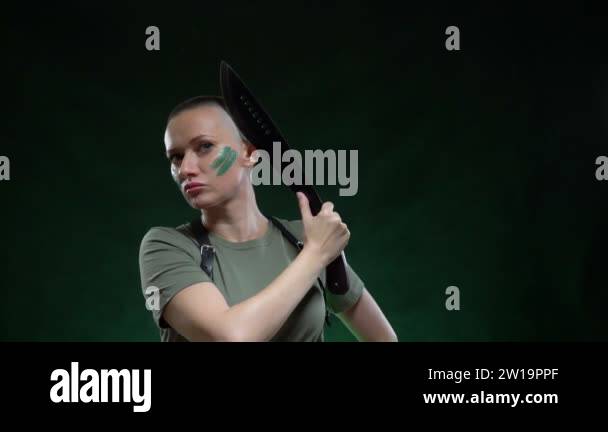 Angry bald girl with camouflage makeup shaving machete hair on a black ...