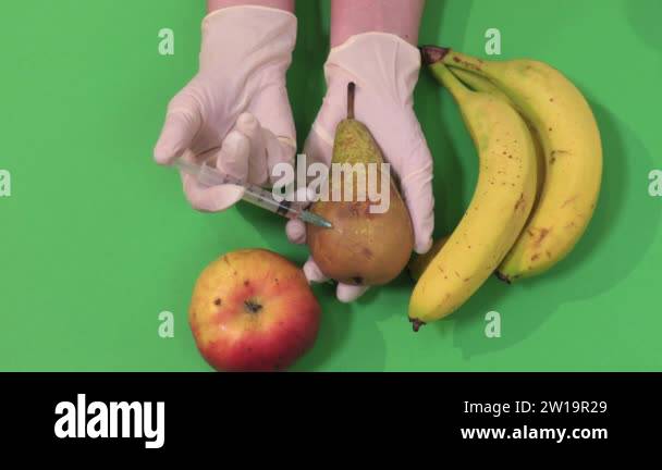 Female scientist hands with syringe injecting into fruits on green ...