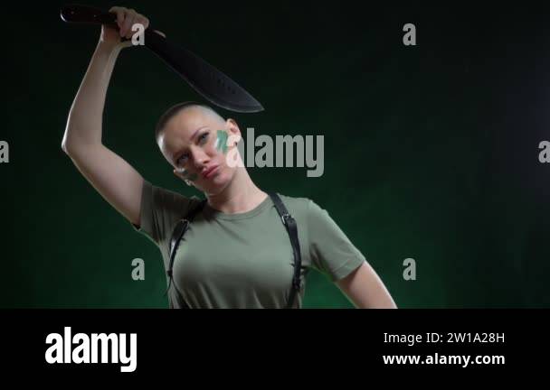 Angry bald girl with camouflage makeup shaving machete hair on a black ...